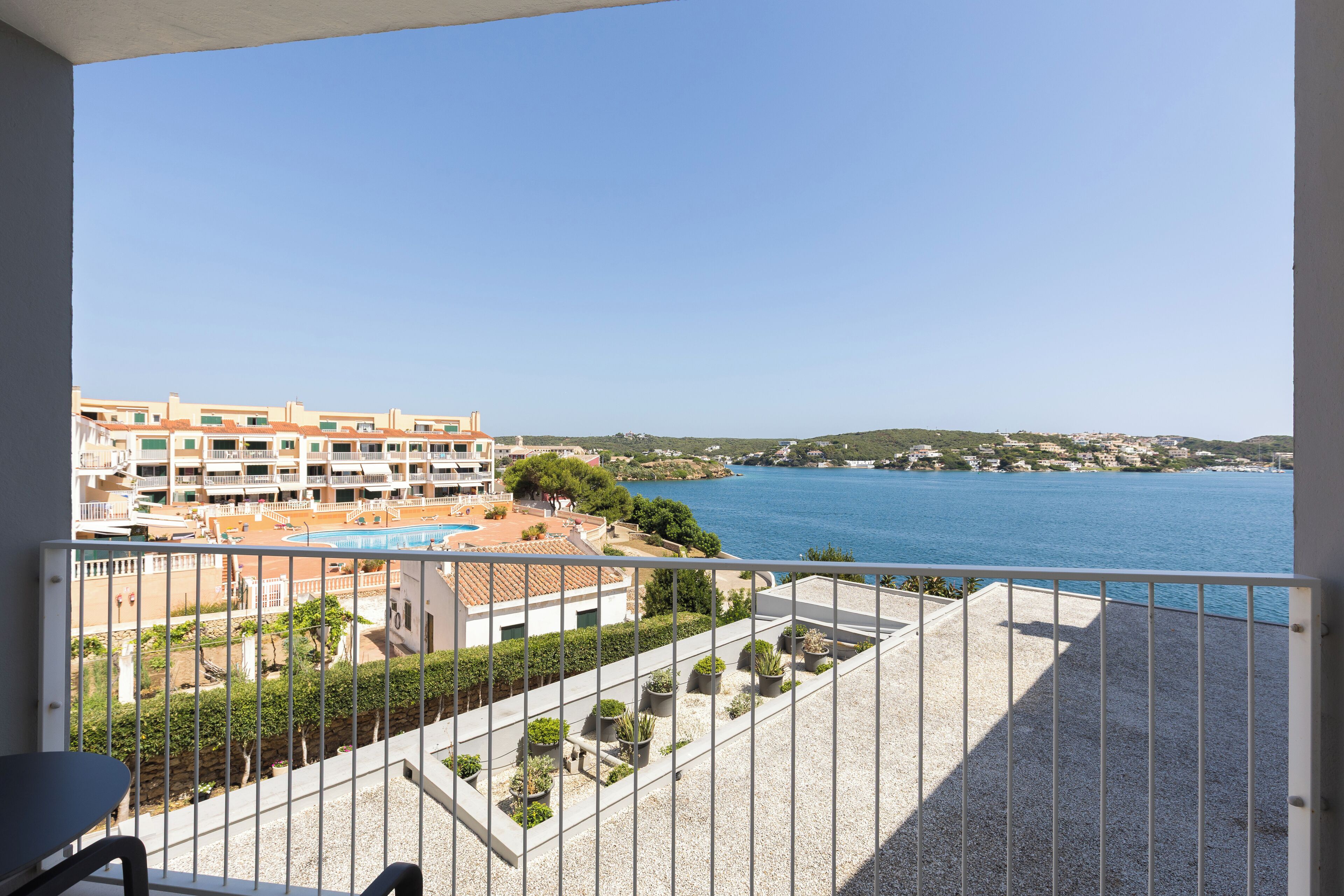Uma varanda com vista para uma cidade costeira, uma piscina e um edifício com várias varandas.