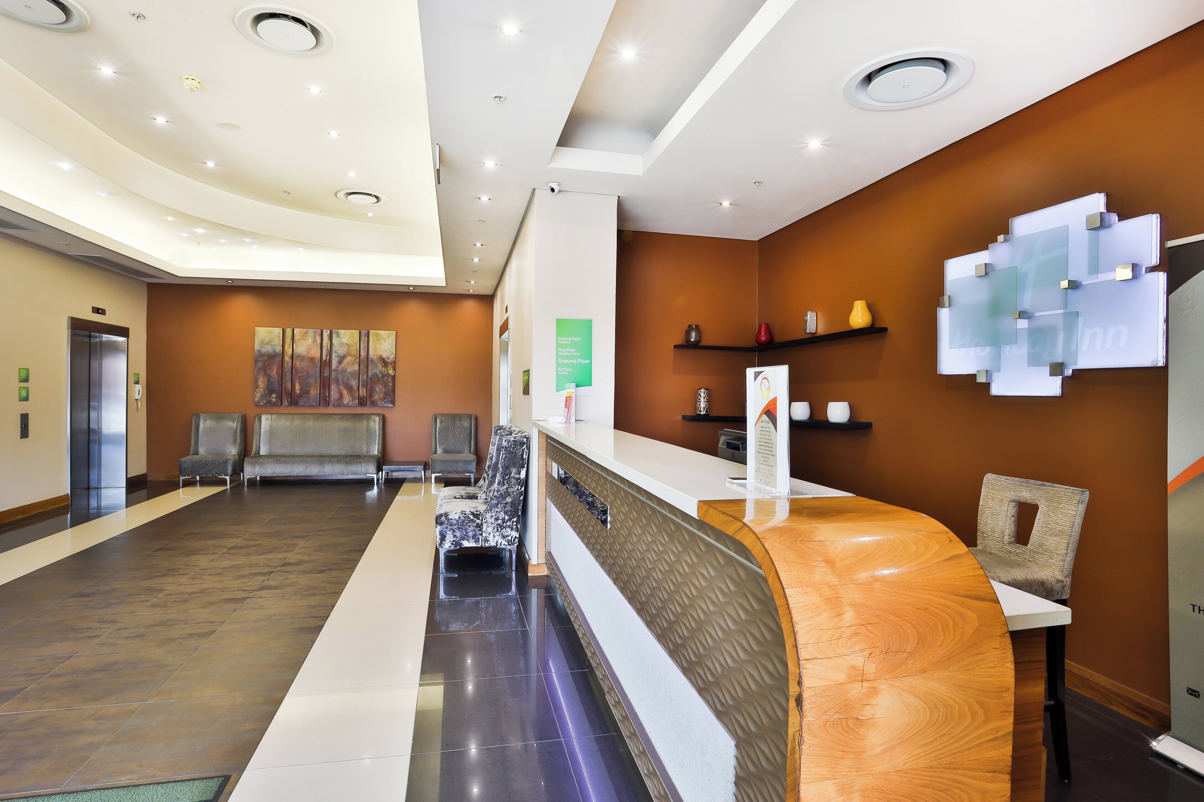 Um hall de hotel com balcão de recepção, área de estar e um painel digital fixado na parede.