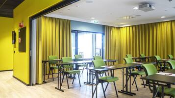 Sala de conferências com paredes amarelas, cadeiras verdes e mesas organizadas para reuniões.