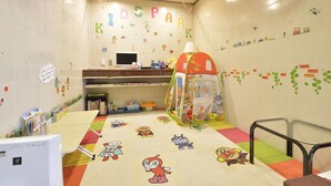 Uma sala de jogos infantil com uma placa 'KIDSPARK', tapetes de brincadeira coloridos e uma tenda de recreação.