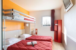 Quarto de hotel com beliches, colcha vermelha, televisão na parede e janela com vista para árvores.