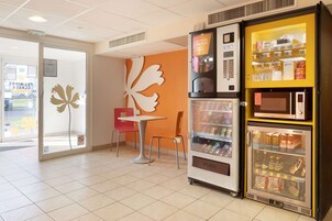 Um interior moderno com uma máquina de vendas automática, entrada por porta de vidro e uma mesa com cadeiras.