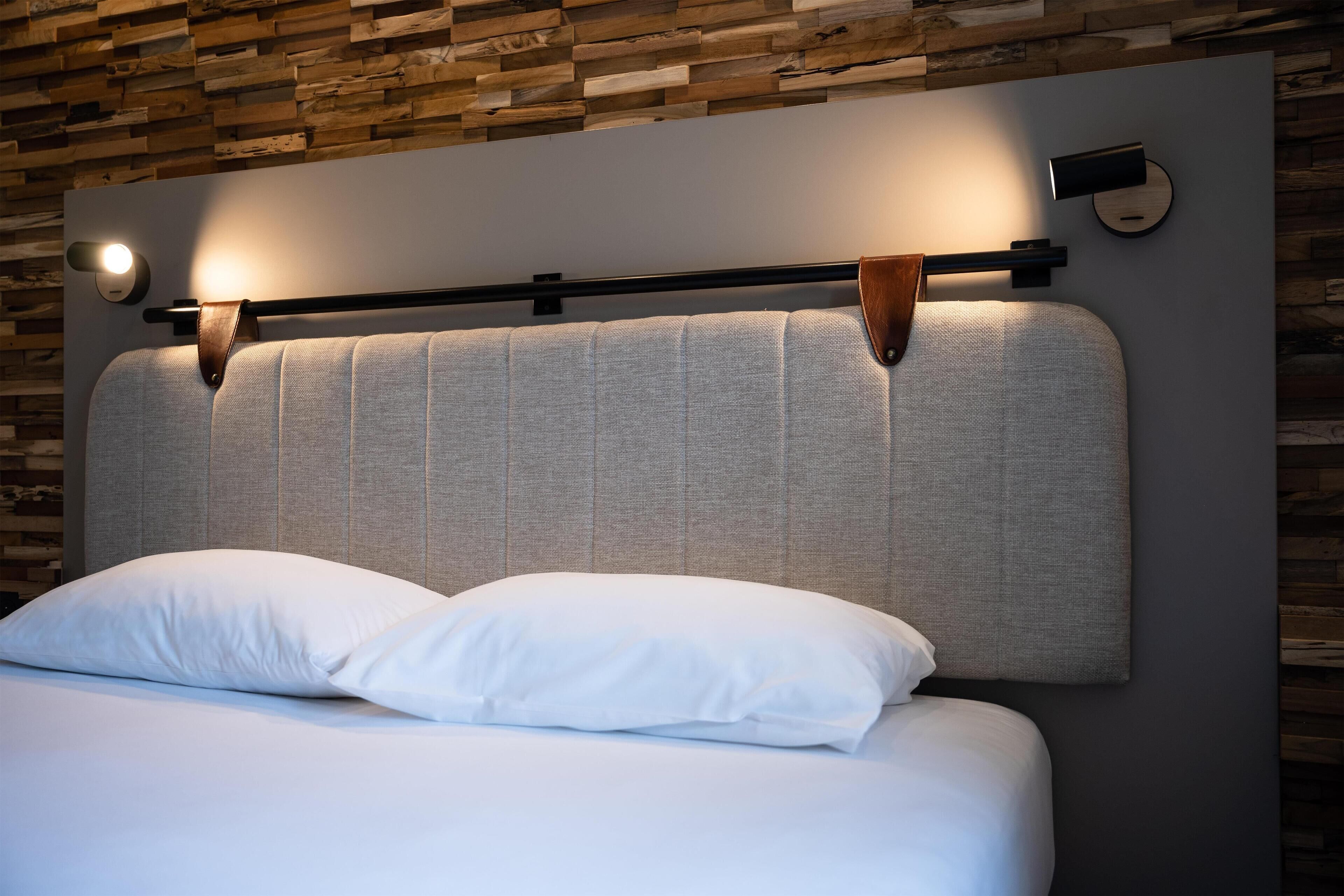 Cama com cabeceira encostada em parede de madeira, duas luminárias laterais e uma TV de tela plana.
