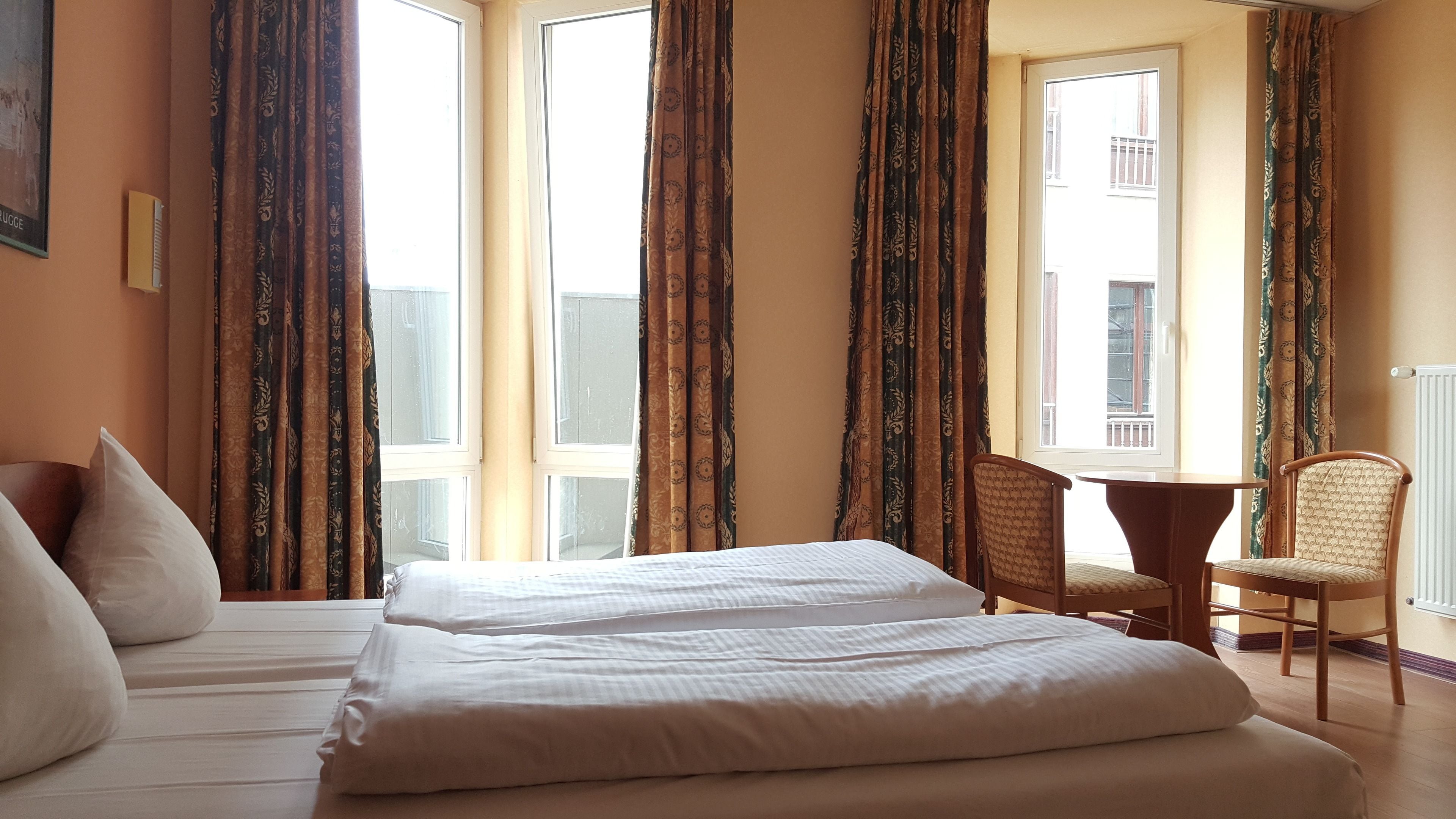 Quarto de hotel com duas camas, uma mesinha e uma cadeira.