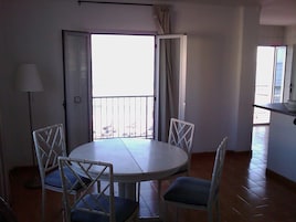 Quarto com uma mesa redonda e quatro cadeiras, uma luminária e varanda com vista.