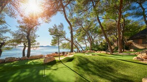 Um campo de golfe bem cuidado, com vista para o mar e montanhas ao fundo.