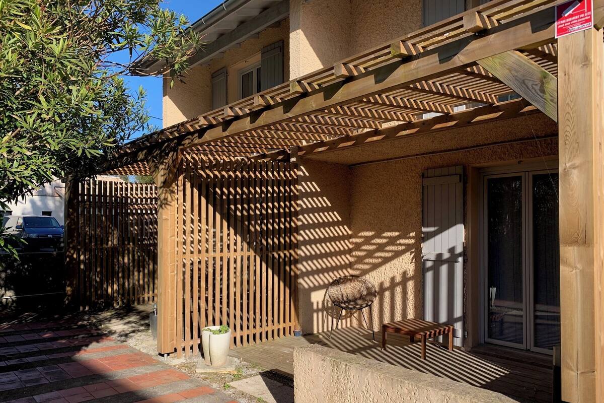 Uma pérgola de madeira com soalho de azulejos e um vaso com planta.