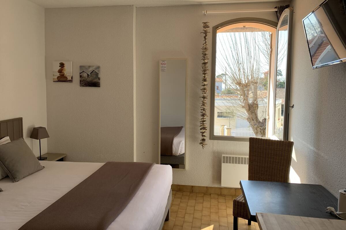 Quarto de hotel com cama, mesa, cadeira, televisão e janela com vista para o exterior.