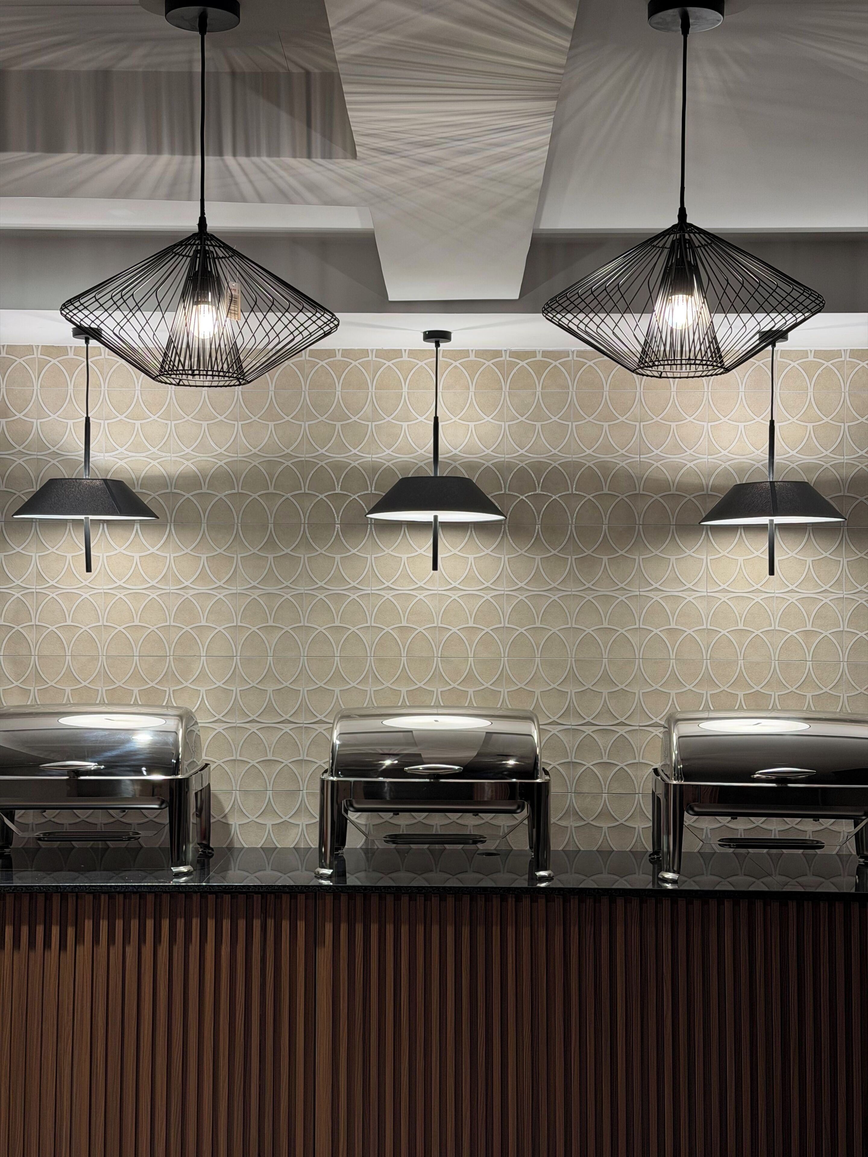 Uma cozinha moderna com três luminárias pendentes, um painel de fundo estampado e uma bancada de madeira.