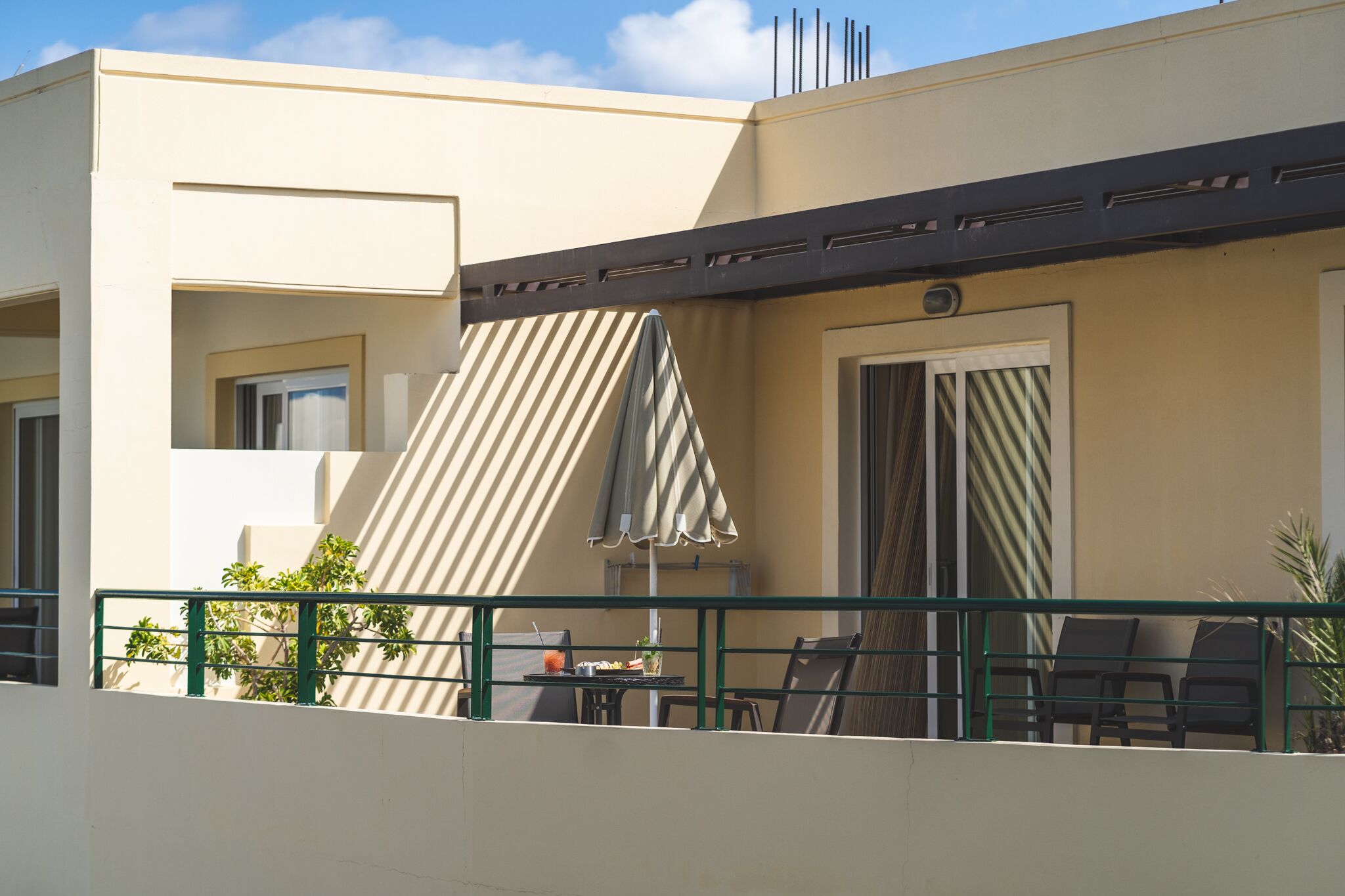 Um edifício moderno com telhado plano, varanda com guarda-corrimão verde e mesa com cadeiras e guarda-sol.