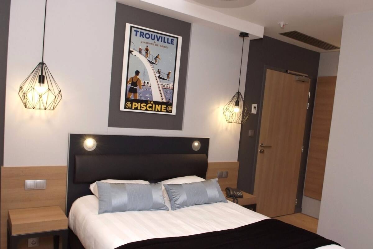Quarto de hotel com uma cama, mesas de cabeceira, um cartaz na parede e luminárias pendentes.