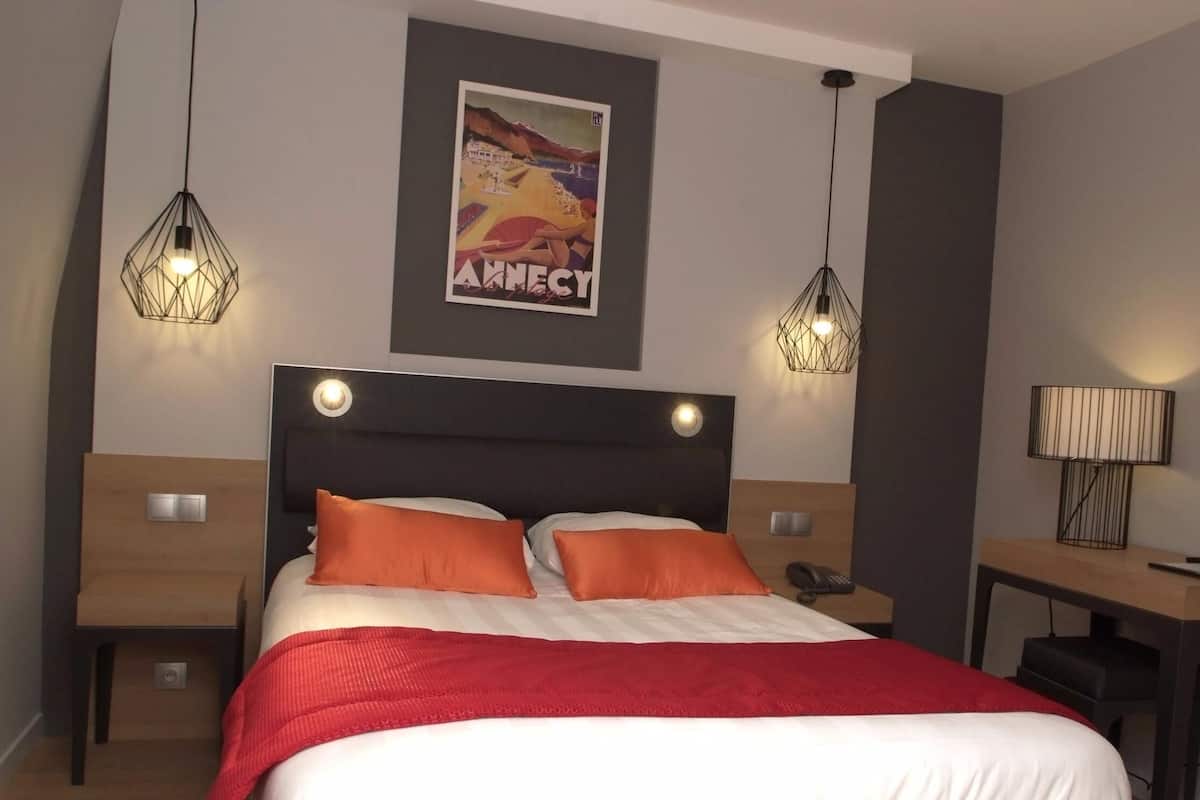 Quarto de hotel moderno com uma cama grande, duas mesas de cabeceira, uma escrivaninha e duas luminárias pendentes.