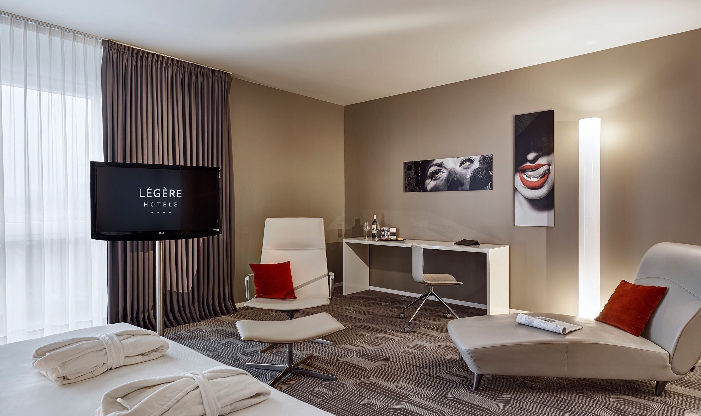 Quarto de hotel com cama, escrivaninha, cadeira, televisão e obras de arte na parede.