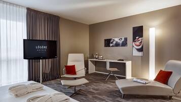 Quarto de hotel com cama, escrivaninha, cadeira, televisão e obras de arte na parede.
