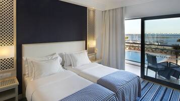 Quarto de hotel com duas camas, uma janela grande com vista para um porto de iates, e uma área de piscina visível pela janela.
