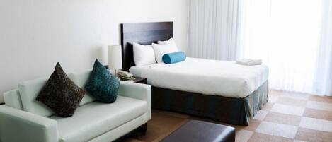 Quarto de hotel com cama, sofá, mesa de cabeceira e um quadro na parede.