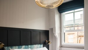 Uma cama bem arrumada com almofadas brancas e escuras, um painel de cabeceira escuro e um lustre suspenso.