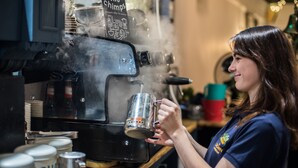 Um barista preparando uma bebida, com vapor saindo da máquina de café.