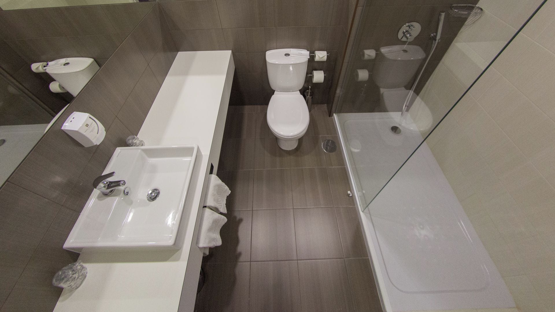 Casa de banho moderna com sanita branca, lavatório e cabine de duche em vidro.