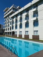 Um hotel moderno com piscina, várias varandas e um céu azul límpido.