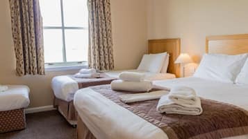 Quarto de hotel com duas camas de solteiro, uma cama maior e uma pequena área de estar.