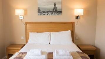 Quarto de hotel com uma cama grande, duas mesas de cabeceira, uma luminária na parede e um quadro emoldurado acima da cama.