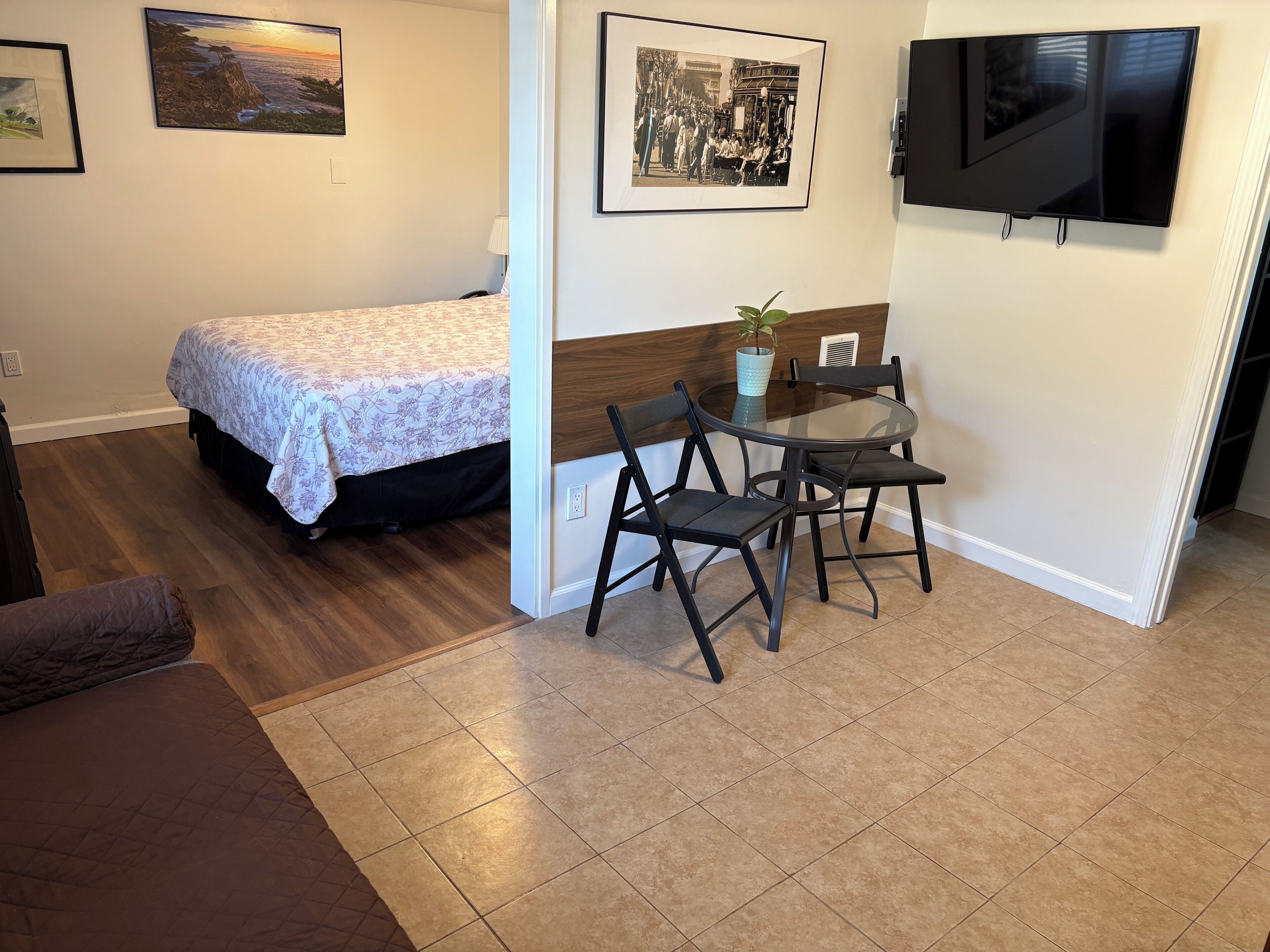 Quarto com cama, uma mesinha com cadeiras, televisão e quadros nas paredes.