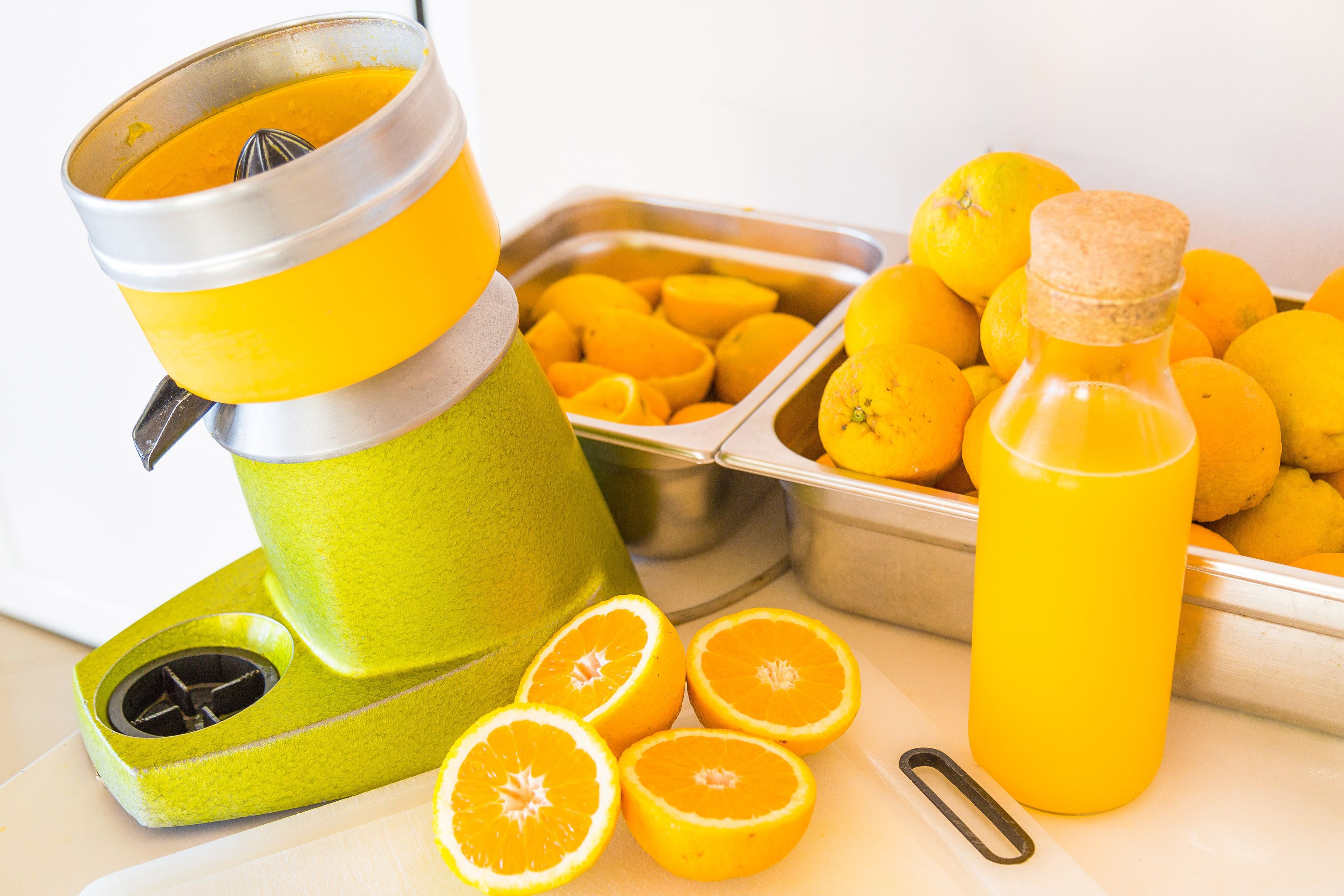 Um espremedor de frutas, laranjas fatiadas e uma garrafa de suco em uma bancada.