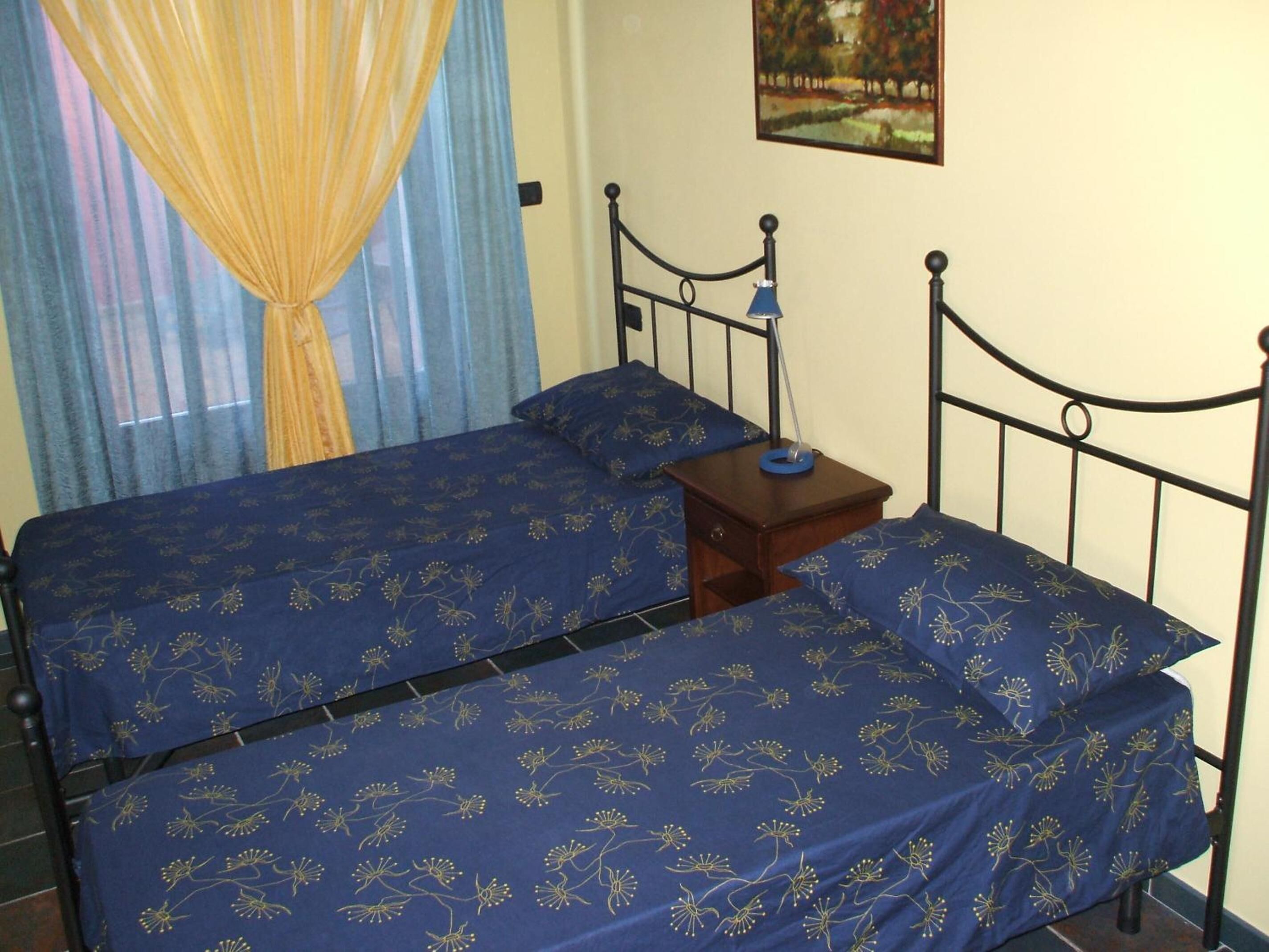 Quarto com duas camas de solteiro, uma mesa de cabeceira, uma luminária e um quadro na parede.