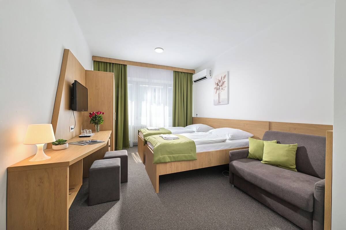 Quarto de hotel com cama, escrivaninha, cadeira, sofá e televisão.