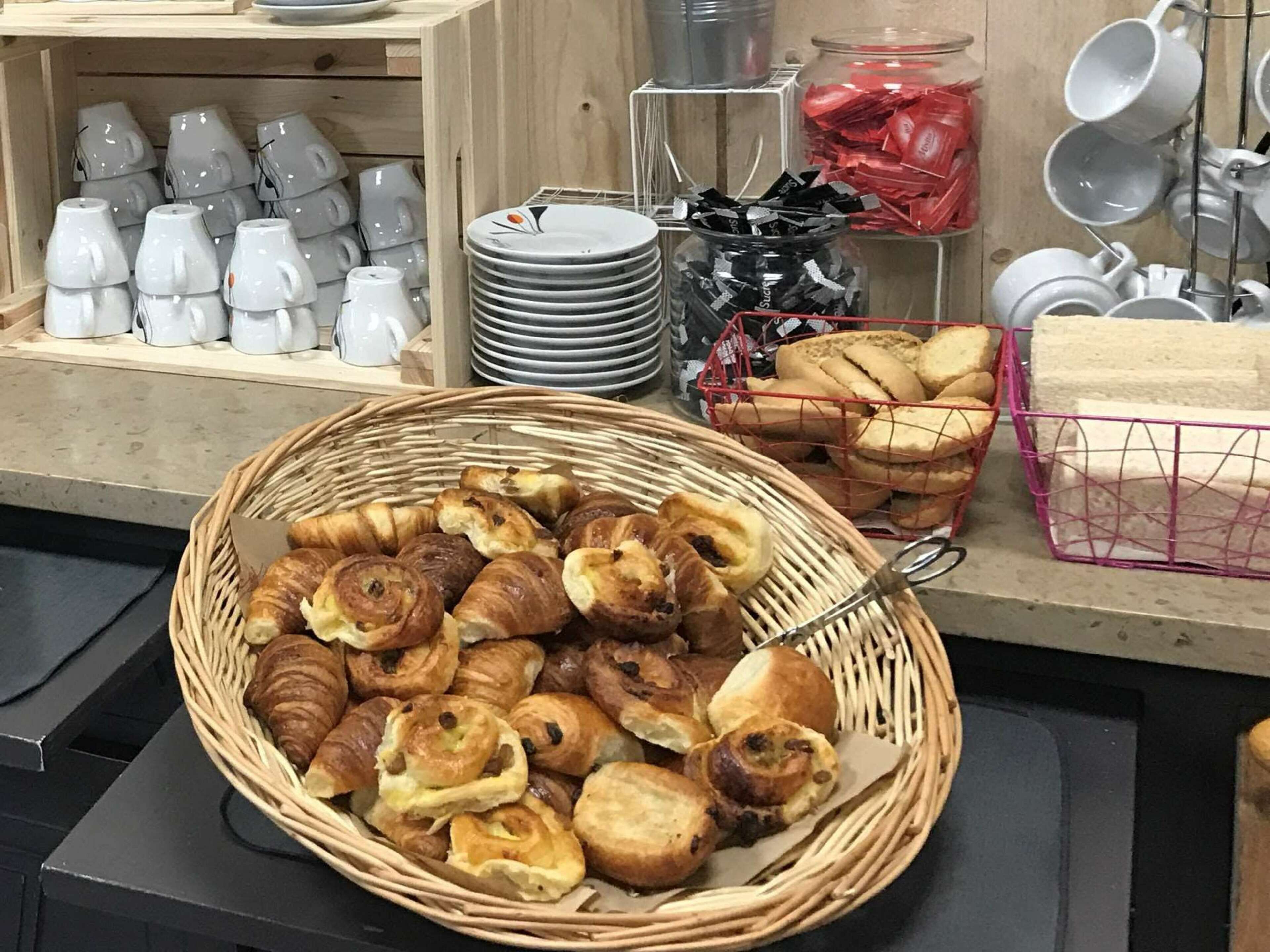 Exposição de diversos produtos de panificação, incluindo croissants e pão, em cestos e prateleiras.