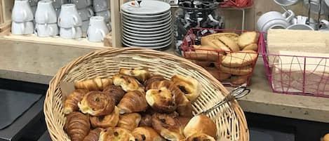 Exposição de diversos produtos de panificação, incluindo croissants e pão, em cestos e prateleiras.