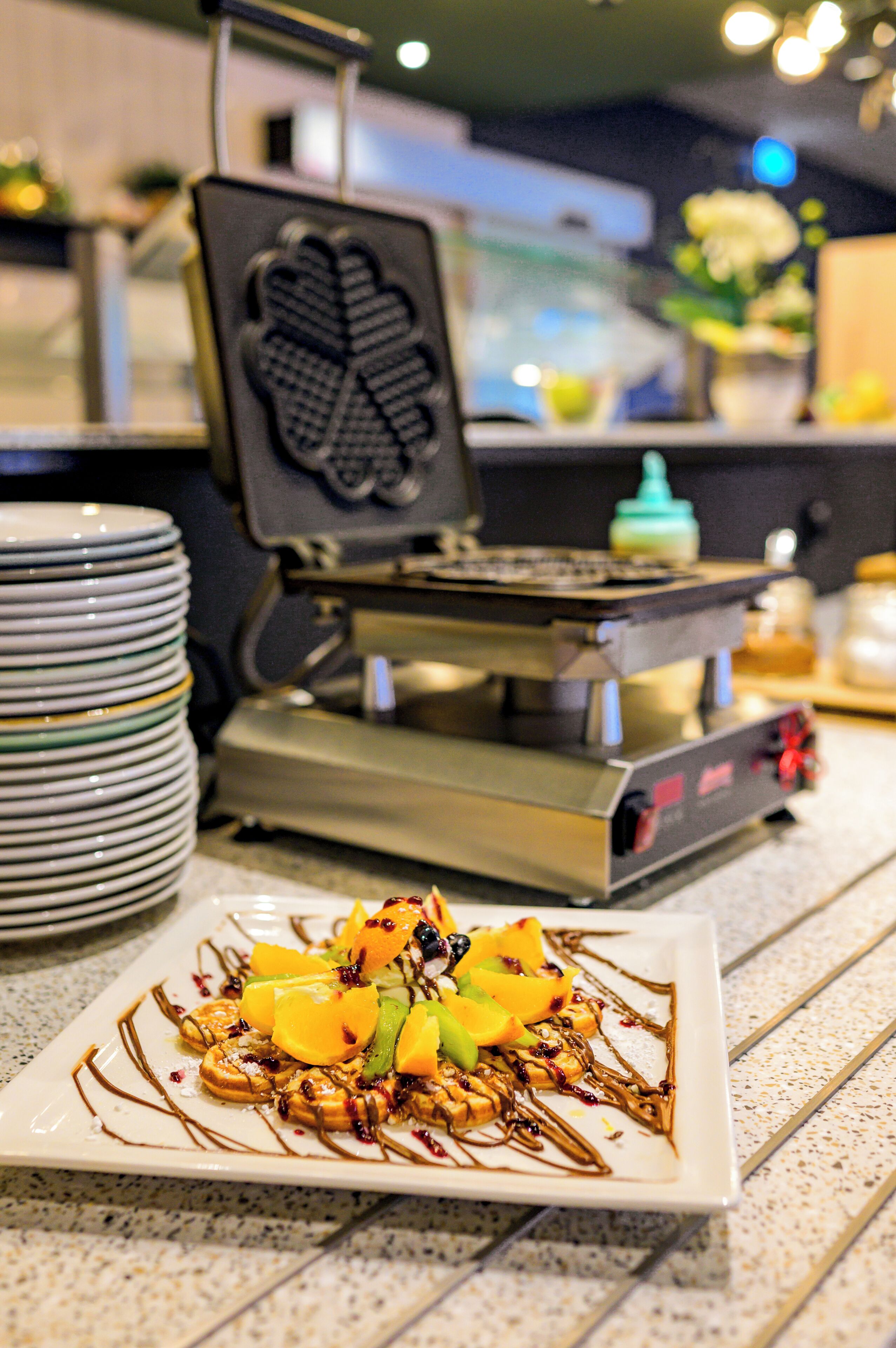 Uma máquina de waffle em uma bancada, com um prato de comida na frente.
