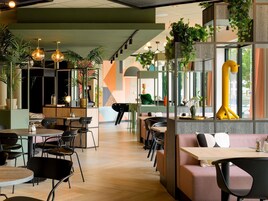 Um café moderno com várias áreas de estar, incluindo mesas e cabines, e uma variedade de plantas.