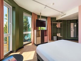 Quarto de hotel com uma cama grande, televisão, escrivaninha e vista para o exterior.