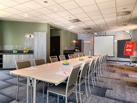 Uma sala de conferências com uma mesa comprida, cadeiras, uma tela de projetor e um letreiro com a mensagem 'SPEAK TO ME'.