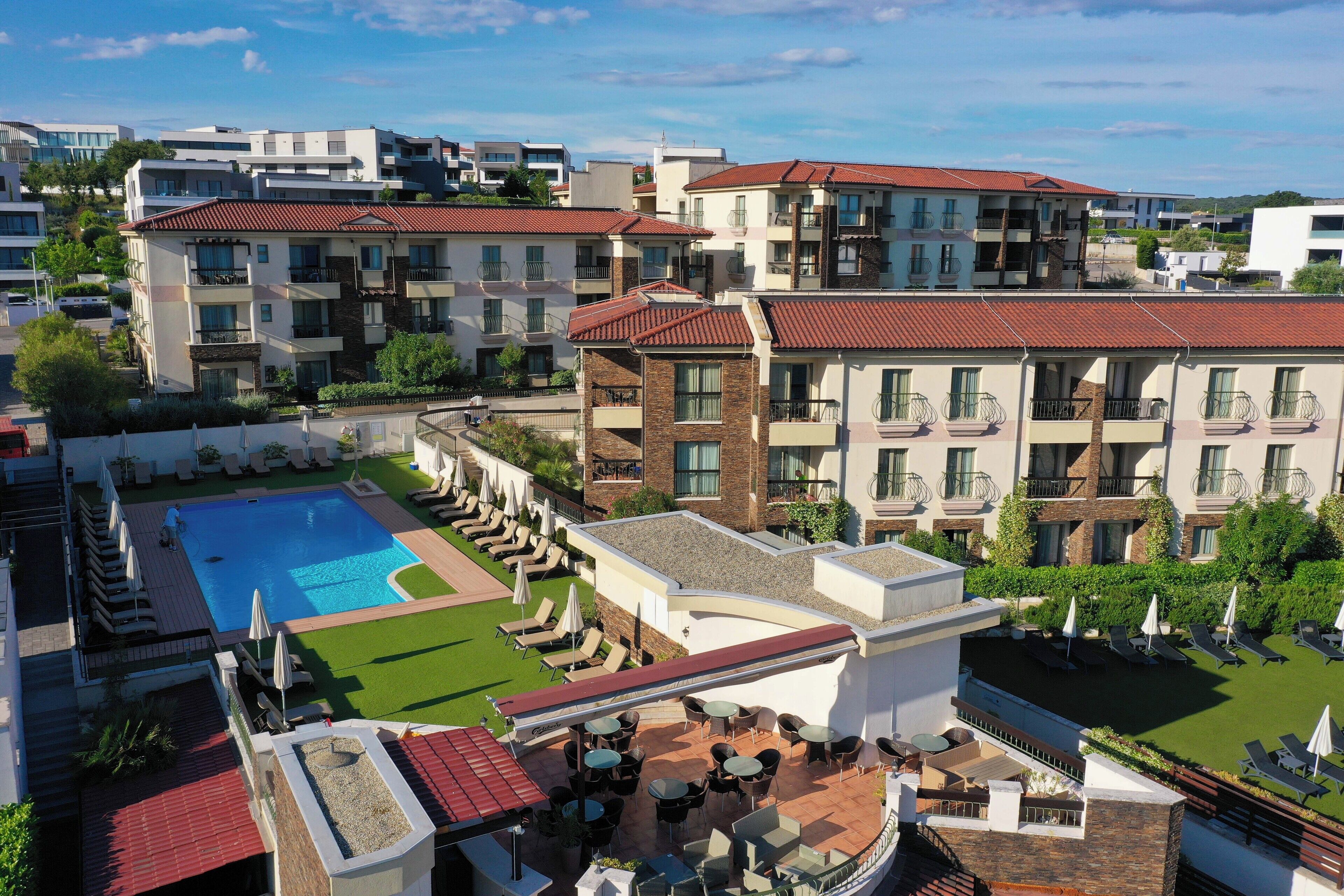 Um hotel com piscina no terraço, área de estar externa e várias varandas.