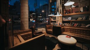 Uma área de estar aconchegante, com assentos de couro, uma mesa de centro de madeira e uma estante repleta de livros.