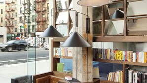 Um espaço de leitura moderno com assentos em couro, uma mesinha de centro e uma estante repleta de livros.