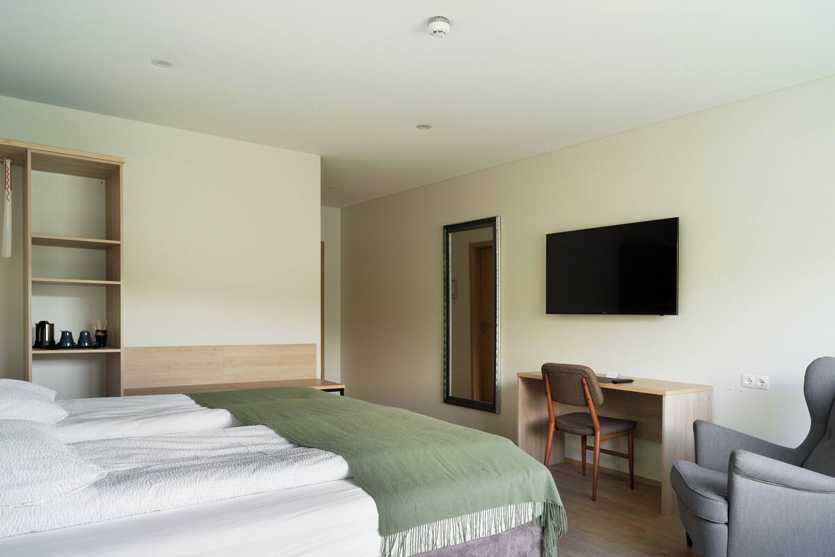 Quarto de hotel com cama, secretária, cadeira, televisão e armário.