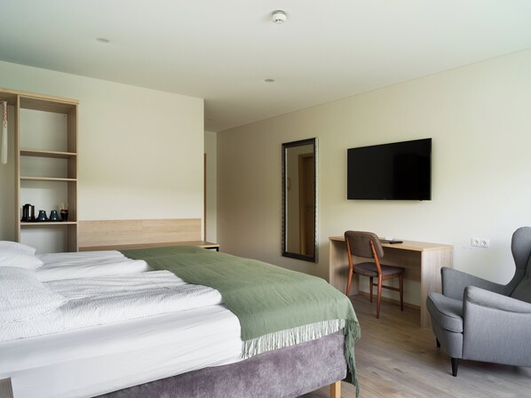 Quarto de hotel com cama, secretária, cadeira, televisão e armário.