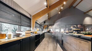 Uma cozinha espaçosa com vigas de madeira, um balcão comprido com alimentos e janelas grandes.