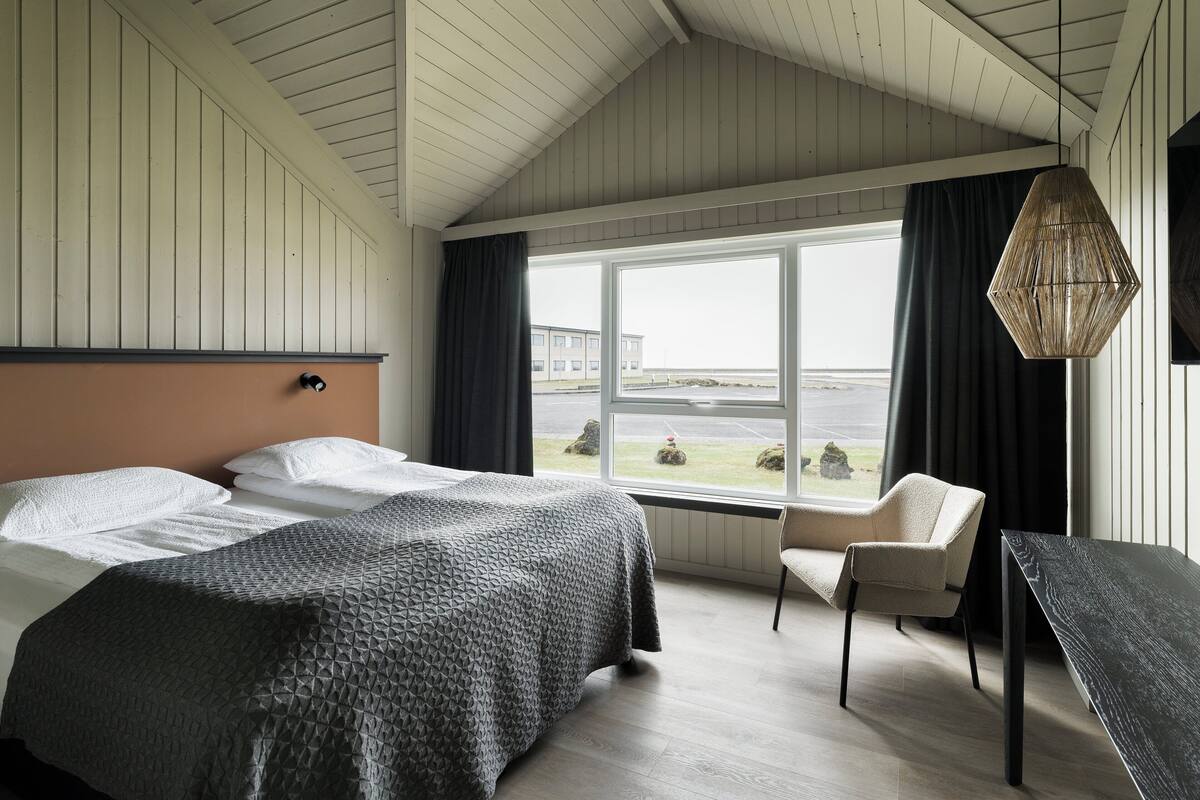 Quarto de hotel com uma cama grande, uma cadeira, uma mesa e janela com vista para o exterior.