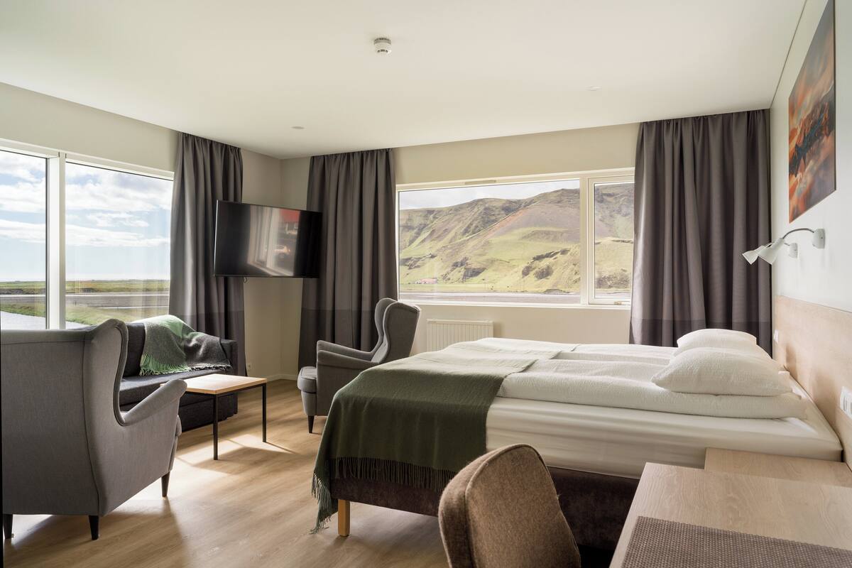Quarto de hotel moderno com cama, escrivaninha, cadeira e televisão.