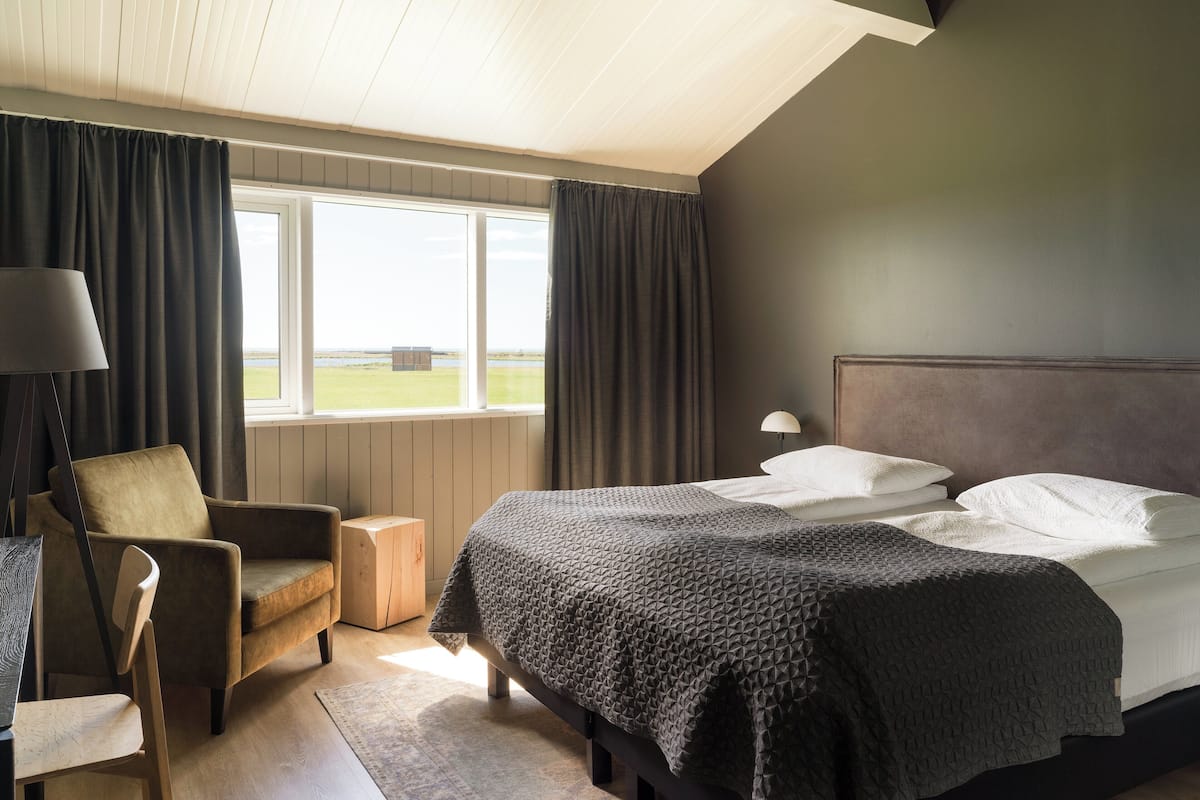 Quarto com cama, cadeira, mesa de cabeceira e janela com cortinas.