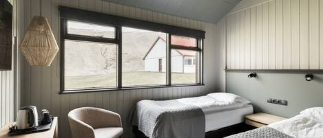 Quarto com duas camas, uma cadeira, escrivaninha com chaleira e janela com vista para uma casa.