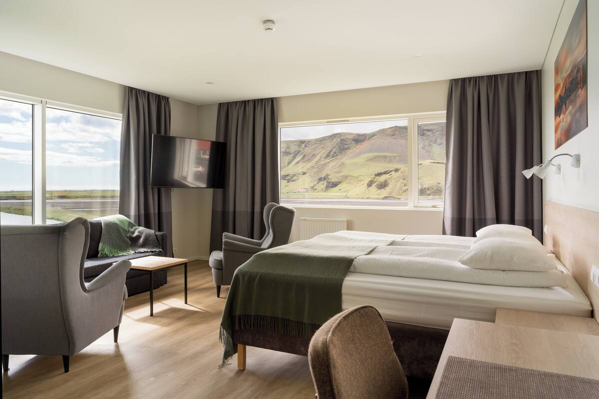 Quarto de hotel moderno com cama, escrivaninha, cadeira e televisão.