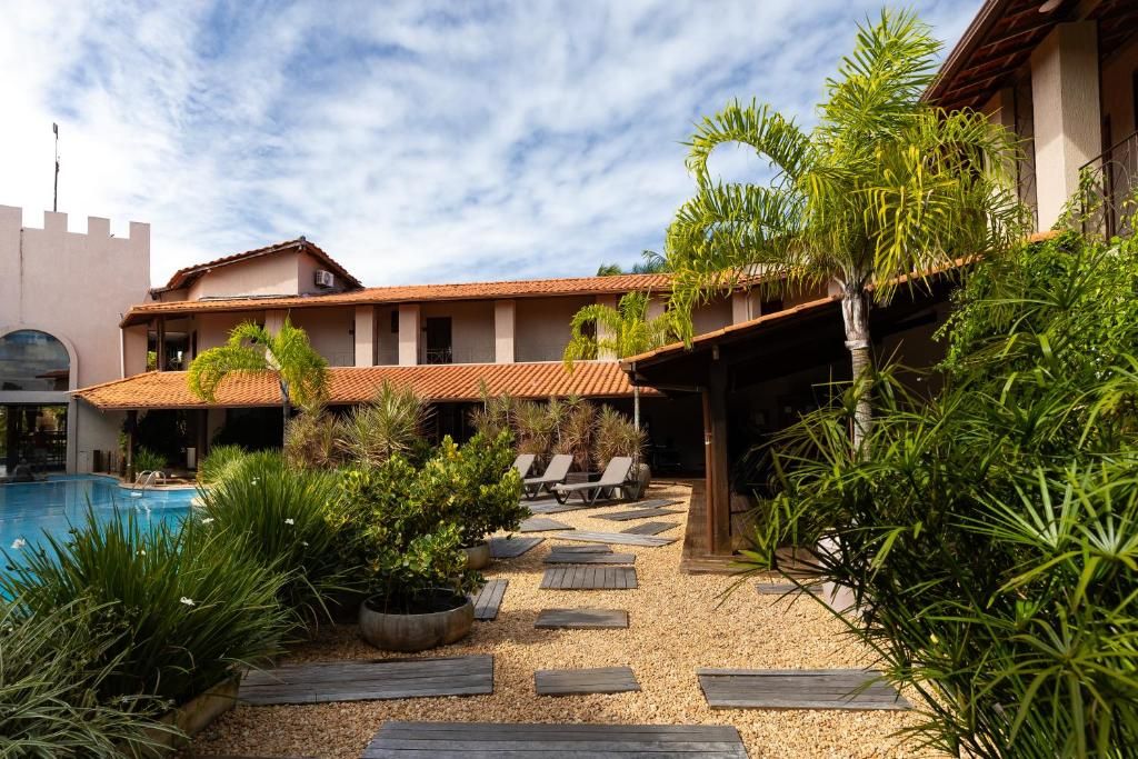 Uma área de piscina com espreguiçadeiras, cercada por plantas tropicais e um edifício com telhado em azulejos.
