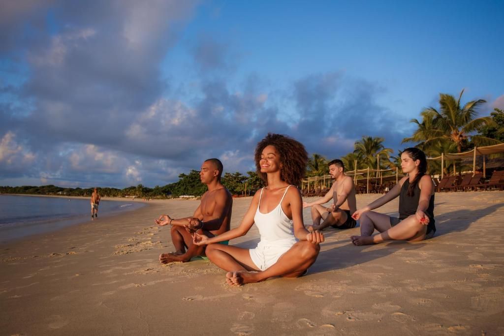 Um grupo de pessoas sentadas em uma praia de areia, com palmeiras ao fundo.