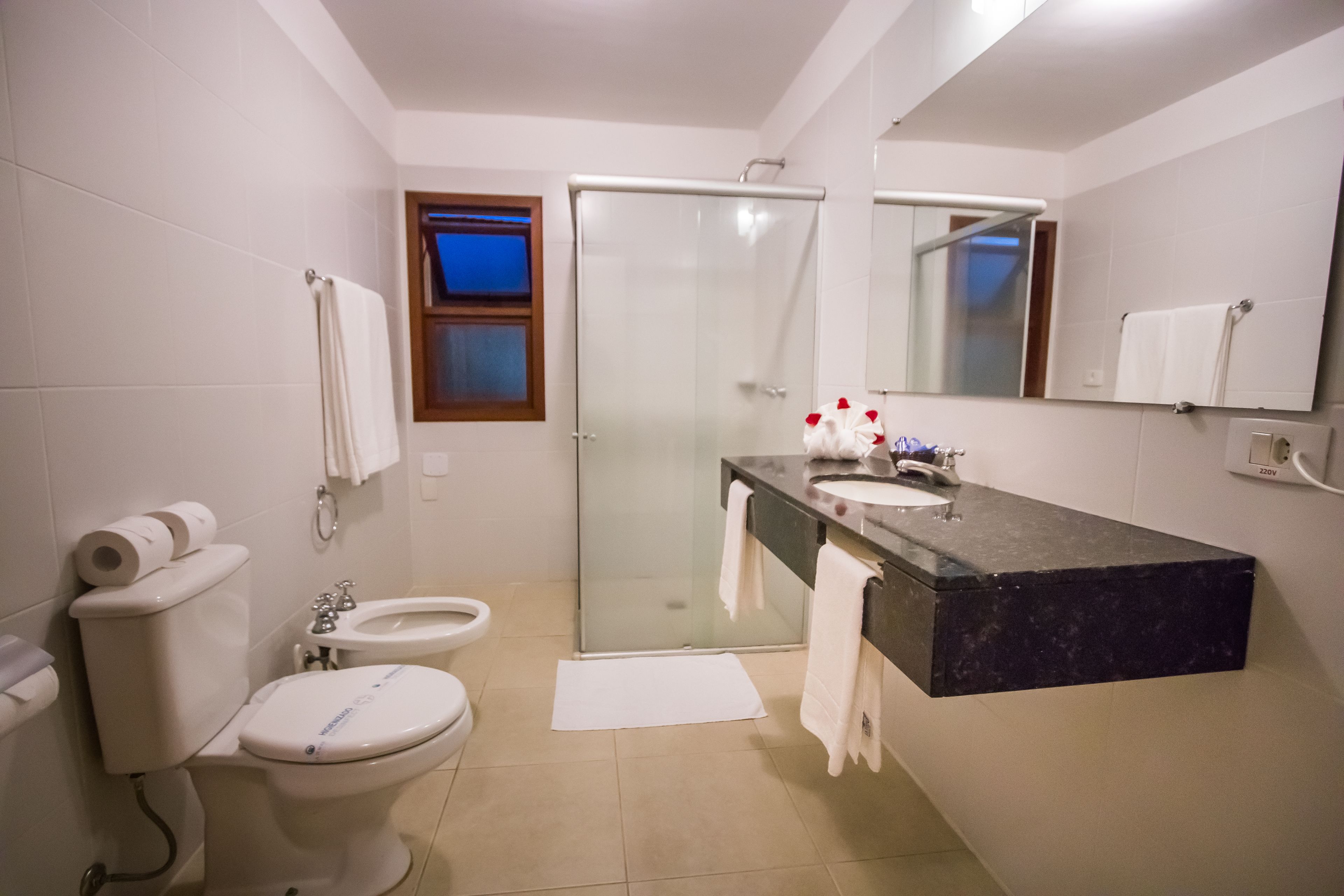 Uma casa de banho moderna com sanita, bidé, lavatório e cabine de duche em vidro.